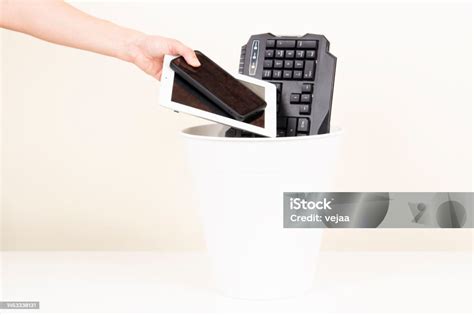 여성의 손은 사용한 디지털 태블릿 컴퓨터와 휴대폰을 오래된 전자 장치로 가득 찬 재활용 쓰레기통에 넣습니다 계획된 노후화 전자 폐기물 재사용 및 재활용 개념을위한 전자