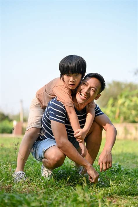 Smiling Asian Dad Playing With His Son In The Backyard While Carrying