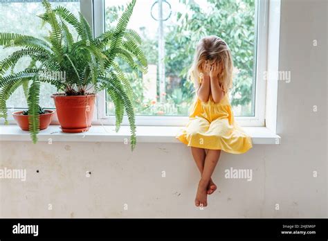 Young Little Crying Girl Barefoot Sitting On Window Sill Face In Hands