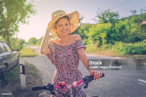 야외 오픈 로드 아스팔트에서 드레스와 모자를 입고 여름 화창한 날에 자전거를 밀어 가는 핸들 바 그립을 들고있는 젊은 여성 거리에 대한 스톡 사진 및 기타 이미지 Istock