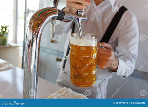 Barman Pours A Light Foamy Beer Into A Large Mug During The Oktoberfest