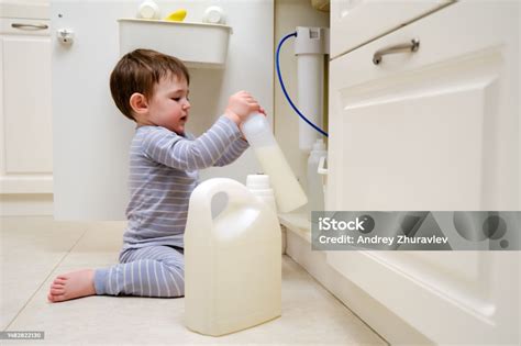 한 아이가 부엌 싱크대 아래에서 화학 세제를 가지고 놀고 있다 아기는 세제가 든 병을 들고 있습니다 2세 정도 정도의 아이