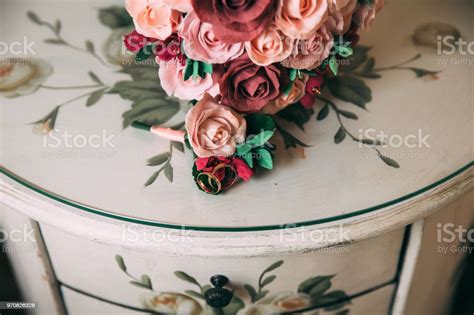 신혼 부부와 신랑의 Boutonniere 골드 반지 나무 빈티지 테이블에 누워 레드와 핑크 장미 웨딩 부케 배경에 놓여 있습니다