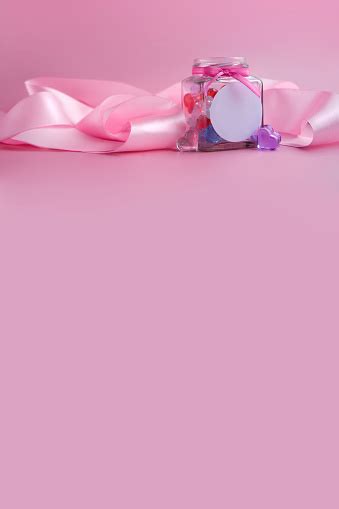 내부의 하트가 있는 유리 항아리와 분홍색 배경에 분홍색 실크 리본이 있습니다 사랑 컨셉과 발렌타인 데이 배너 모캡 세로