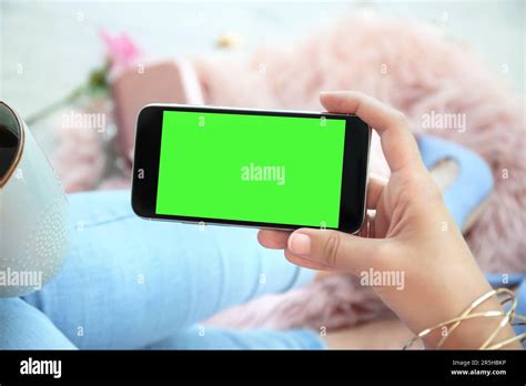 Chroma key compositing. Woman holding smartphone with green screen indoors, closeup. Mockup for ...