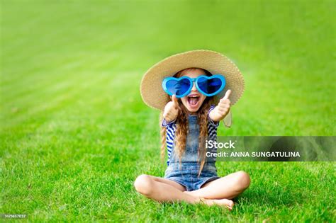 여름에 잔디밭에서 큰 재미있는 선글라스와 푸른 잔디에 밀짚 모자를 쓴 쾌활한 어린 소녀가 수업 텍스트 공간을 보여주는 재미와 기쁨을 누리고 있습니다 아이에 대한 스톡 사진