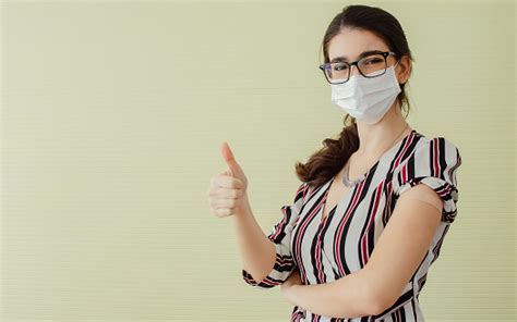 얼굴 가면을 쓰고 포즈를 취하고 엄지 손가락을 들고 어깨에 플라스틱 붕대를 가진 바이러스를 예방하고 노란 배경에 공간을 복사하는 것을 예방 접종하고 있는 인물 백인 젊은