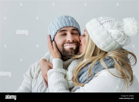 Happy Blonde Woman In Knitted Hat Kissing Cheek Of Smiling Boyfriend