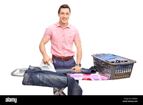 Cheerful Young Man Ironing A Pair Of Jeans On An Ironing Board And