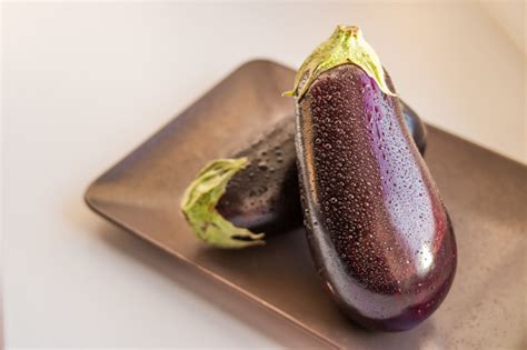 젖은 가지의 클로즈업 보기 Aubergines 과일 드롭 흰색 배경에 접시에 절연 물 물 방울으로 원시 가지입니다 젖은 신선한