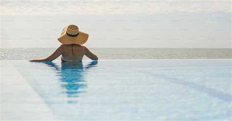 모자를 쓴 아름다운 여자가 푸른 수영장의 가장자리에서 휴식을 취하고 여름 휴가와 바다 전망을 즐기고 있다 날씬한 젊은 여성이 수영장의 열대 리조트에서 휴식을 취하고 있다