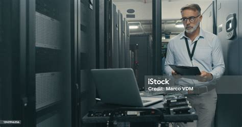 데이터 센터에서 작업하는 동안 디지털 태블릿과 노트북을 사용하는 성숙한 남자의 샷 데이터 센터에 대한 스톡 사진 및 기타 이미지