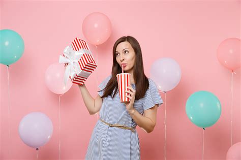 블루 드레스 선물 빨간색 상자를 들고 찾고 예쁜 여자의 초상화 선물 마시는 소 다 또는 콜라 파스텔 핑크 배경에 플라스틱 컵에서
