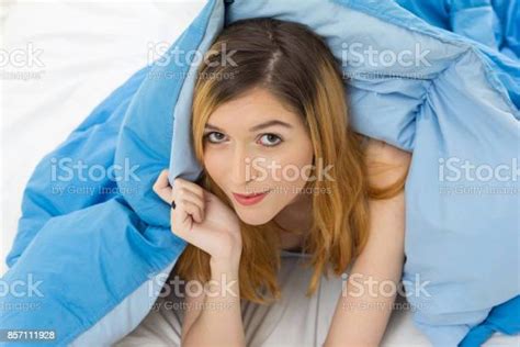 여자는 그녀의 얼굴에 약간의 미소를가지고 그녀는 파란이 불 침대입니다 아침 게으름과 휴식의 개념입니다 관능에 대한 스톡 사진 및