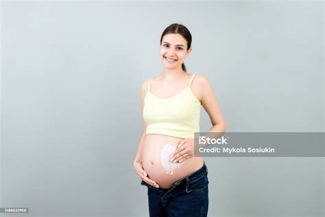 그녀의 배에 스킨 케어 크림을 적용 열린 청바지에 임신 한 여성의 클로즈업 복사 공간과 다채로운 배경에서 스트레치 마크를