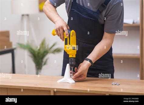 Skilled Carpenter In Blue Overalls Using Yellow Electrical Drill