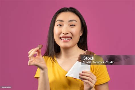 초콜릿을 먹고 맛있는 디저트를 즐기고 카메라를 보며 웃고 보라색 스튜디오 배경 위에 서 있는 행복한 한국 여성 20 24세에