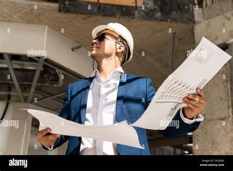 Man Architect Wearing Formal Suit And Hard Hat During Building Construction Control Holding A