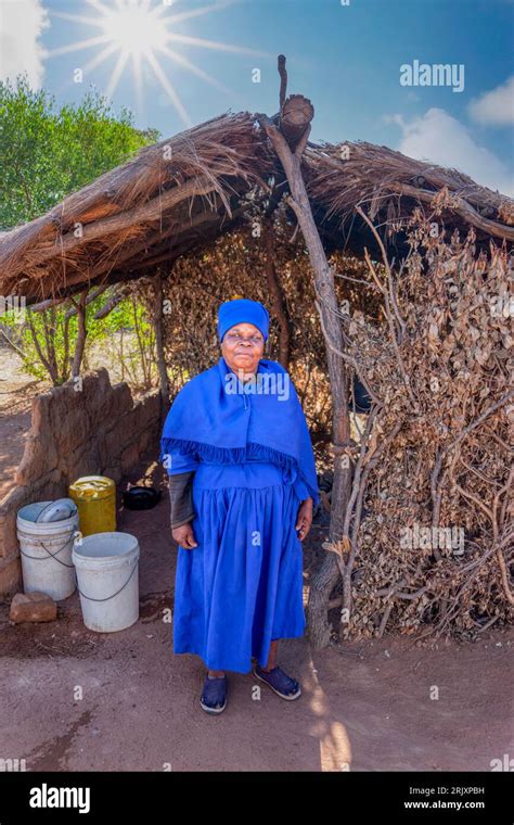 African Old Woman In A Blue Dress Sited In Front Of Her Outdoors