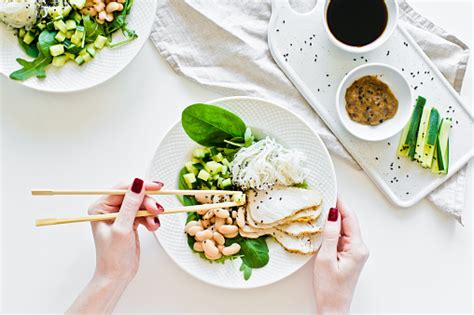 오이의 한 조각에 젓가락을 쥐고 있는 소녀 유리 국수 콩 닭 가슴살 시금치 Arugula와 오이를 가진 부처님 그릇 흰색 배경 평면도 텍스트 공간 건강한 식생활에 대한 스톡