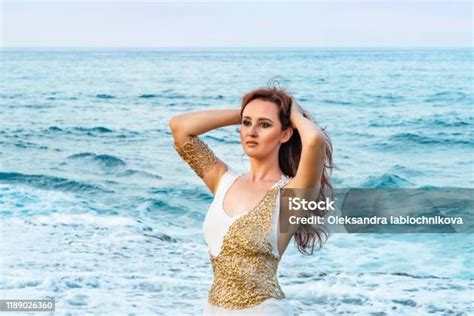바다 배경에 흰색과 황금 옷을 입고 긴 머리를 가진 젊은 여성 그녀의 머리를 만지고 멀리 찾고 공간을 복사 고요한 장면에 대한 스톡 사진 및 기타 이미지 Istock