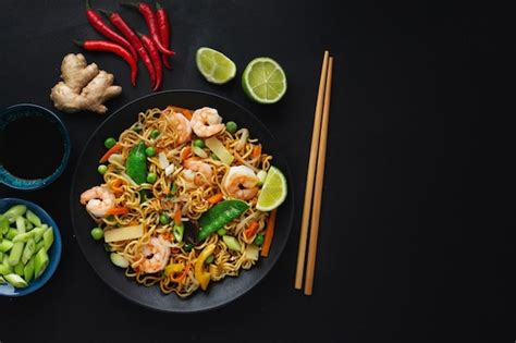 Азиатская лапша с креветками и овощами подается в миске на темном фоне ...