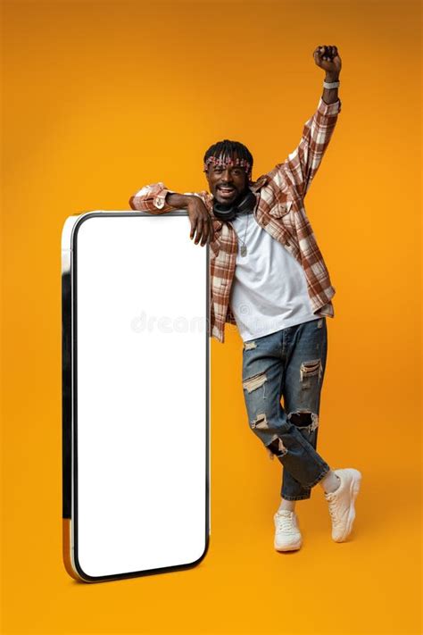 smiling african man standing near huge smartphone with blank screen on