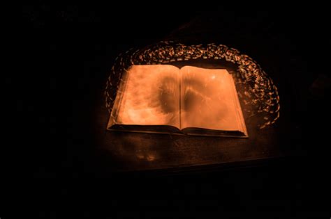 반짝이는 황금색 배경이 있는 나무 탁자 위에 열린 고대 책의 그림책을 상상해 보십시오 마법의 힘으로 마법 빛나는 책 주위 번개