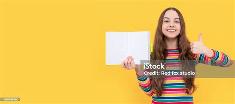 행복한 아이는 복사 공간 노란색 배경을위한 열린 책을 들고 손 제스처를 엄지 손가락으로 주며 만족합니다 여학생 학생의 수평 고립 포스터 여학생의 배너 헤더 초상화 복사 공간