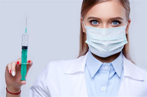 고립된 배경에 주사기를 들고 유니폼과 의료 보호 마스크를 착용하는 여성 의사 젊은 간호사 병원 직원 간호사에 대한 스톡 사진 및