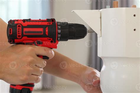 Man Assembling White Table Furniture At Home Using Cordless Screwdriver