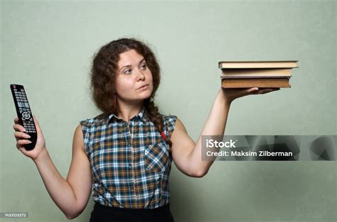 책 대 텔레비전 한 여성이 한 손에 든 책과 다른 한 손의 Tv 리모컨 중에서 선택합니다 Tv 보기에 대한 스톡 사진 및 기타