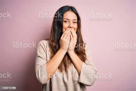 젊은 아름다운 갈색 머리 여자 캐주얼 스웨터를 입고 분홍색 배경 웃음과 부끄러운 웃음 손으로 입을 덮고 험담과 스캔들 개념