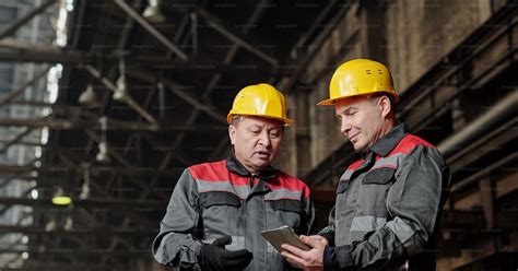 작업복을 입은 두 명의 육체 노동자가 디지털 태블릿을 사용하고 공장에 서서 작업에 대해 논의하고 있다 사진 Unsplash의 노동 이미지