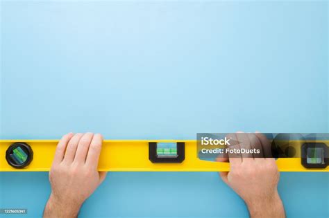 밝은 파란색 테이블 배경에 노란색 정신 수준을 들고 남자 손 바닥 벽 천장 또는 기타 표면 레벨 정밀도를 위한 빌딩 도구 시점