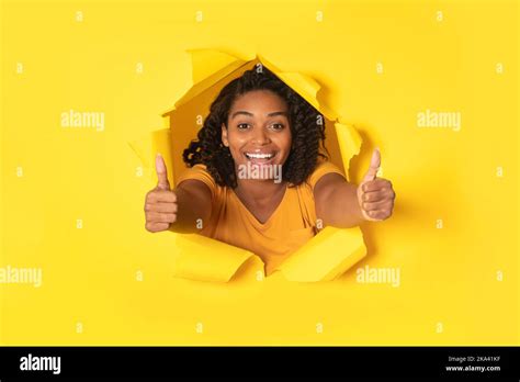 Black Lady Gesturing Thumbs Up Through Torn Paper Yellow Background