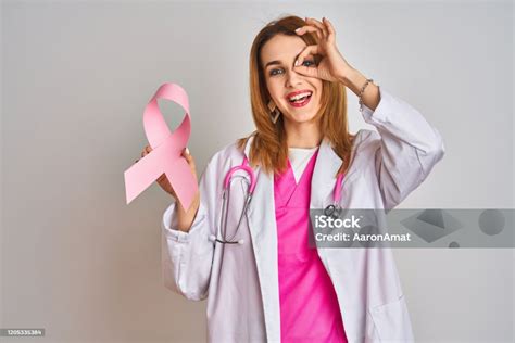 빨간 머리 백인 의사 여자 들고 핑크 암 리본 위에 고립 된 배경 과 행복한 얼굴 웃고 있는 확인 기호 와 눈으로 눈을 통해 보고 개념에 대한 스톡 사진 및 기타 이미지