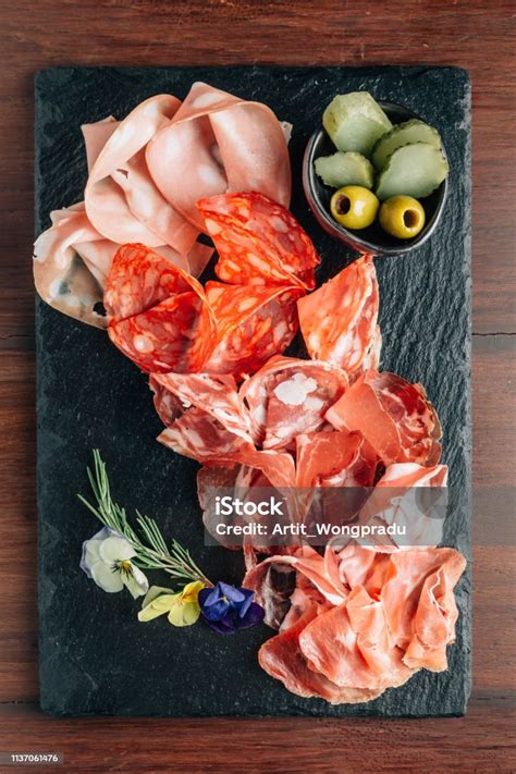Prosciutto와 돌 접시에 차가운 인하 베이컨 살라미와 소시지는 나무 배경에 Wth 꽃 장식 고기 플래터 애피타이저는 채소
