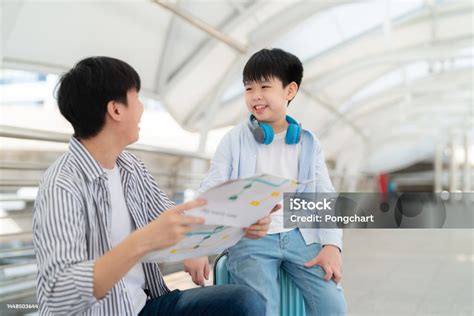 화창한 날 하늘 산책에서 아버지와 함께 수하물에 앉아 헤드폰을 착용한 아시아 소년 아버지는 철도 지도를 들고 있고 아들은 아빠를