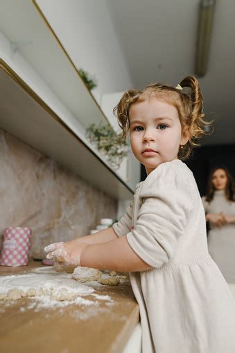 어린 엄마와 함께 식탁 위에서 페이스트리나 파이를 요리하는 어린 아이 엄마와 아이는 반죽을 반죽하고 피자를 요리하고 쿠키 만두 또는 크로와상을 굽습니다 가정 레크리에이션 및