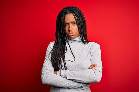 빨간 고립 된 배경 회의론과 긴장 교차 된 팔로 얼굴에 표정을 거부 하는 위에 터틀넥 스웨터를 입고 젊은 아프리카 계 미국인 여성 부정적인 사람 땋은 머리에 대한 스톡 사진