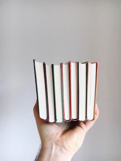 Premium Photo Cropped Hand Of Man Holding Books Against Wall