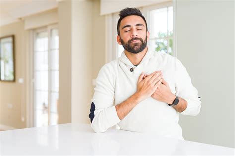 집에서 캐주얼 한 흰색 스웨터를 입은 잘 생긴 히스패닉 남자는 닫힌 눈과 얼굴에 감사 제스처와 가슴에 손을 미소 건강 개념 감사에 대한 스톡 사진 및 기타 이미지 Istock