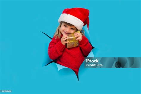 빨간 스웨터를 입은 행복한 미소 짓는 아이와 찢어진 종이 구멍을 통해 크리스마스 선물을 들고 있는 산타 레드 모자 찢어진 종이의 효과 크리스마스 판매 감정에 대한 스톡 사진