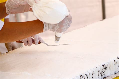 맛 있는 컵 케 잌은 버터 크림으로 장식 하는 제과 과자 장 수의 큰 축제 케이크 스펀지 케이크에 휘 핑된 크림의 흰색 크림을 넣어 흰 장갑에 있는 손 달콤한 음식에 대한