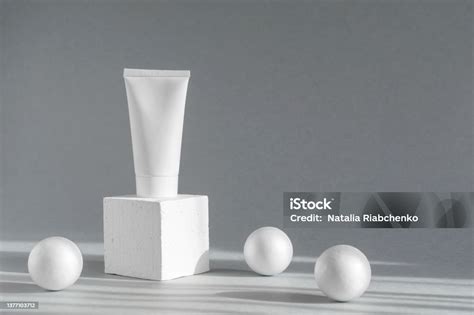 기하학적 3d 연단에 화장품 흰색 튜브의 모형 크림 로션 치약용 플라스틱 용기가 구체로 둘러싸인 정사각형 스탠드에 있습니다
