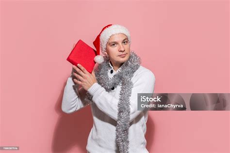 흰색 스웨터와 빨간 산타 모자를 입은 남자가 빨간색 상자를 흔들어 어떤 선물이 있는지 알아보십시오 겨울에 대한 스톡 사진 및