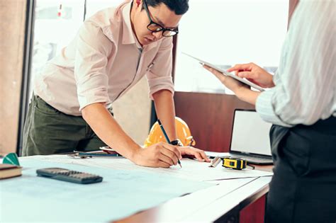 건물을 가리키는 펜을 들고 건설 계획을 작성하는 엔지니어는 세부 사항을 가진 건축업자를위한 가이드로 작성합니다 설계 및 쓰기 청사진 2명에 대한 스톡 사진 및 기타 이미지