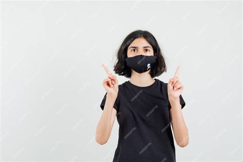 검은 티셔츠 마스크를 가리키고 현명한 찾고 어린 소녀 전면보기 무료 사진