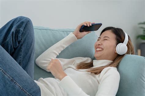 무선 헤드폰을 끼고 즐거운 젊은 아시아 여성들이 앉아서 음악을 즐기고 재미있게 놀고 음악을 듣고 팔을 들고 좋아하는 노래에 맞춰
